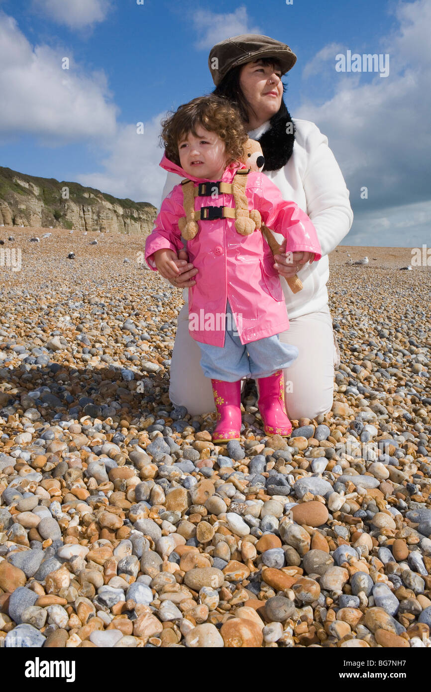 A mother and her daughter wearing a pink mac coat on a pebble beach on ...