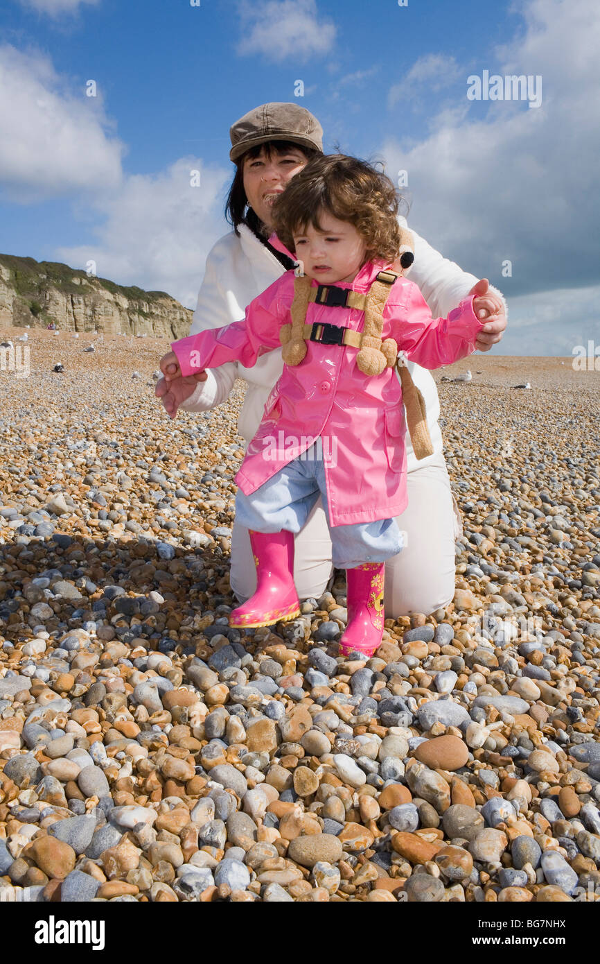 A mother and her daughter wearing a pink mac coat on a pebble beach on ...