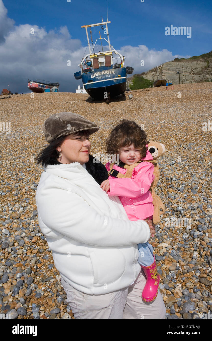 A mother and her daughter wearing a pink mac coat on a pebble beach on ...