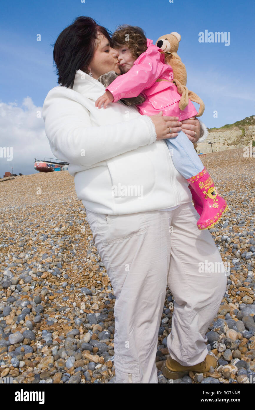 A mother and her daughter wearing a pink mac coat on a pebble beach on ...