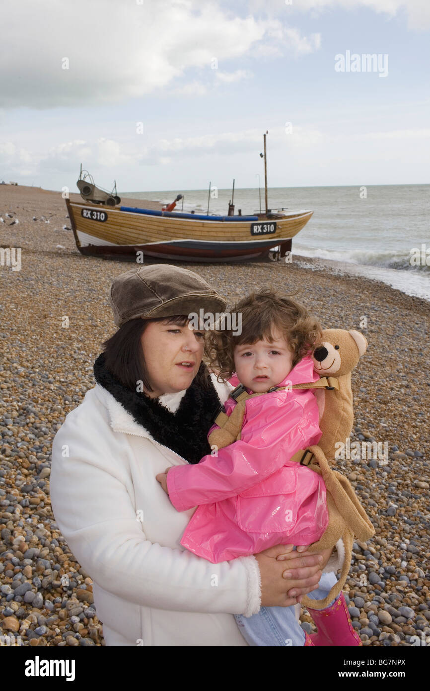 A mother and her daughter wearing a pink mac coat on a pebble beach on ...