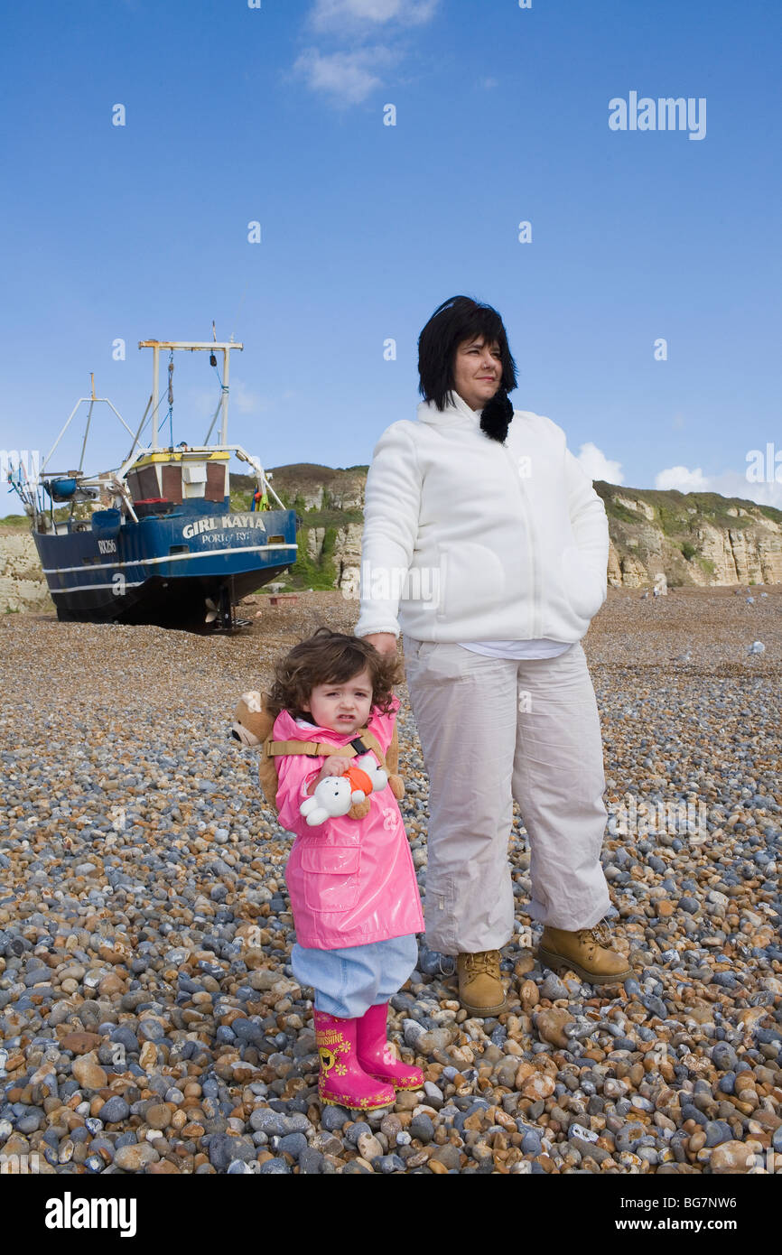 A mother and her daughter wearing a pink mac coat on a pebble beach on ...