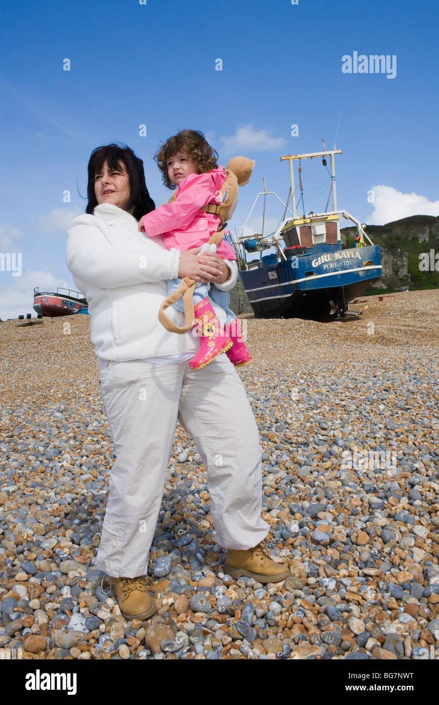 A mother and her daughter wearing a pink mac coat on a pebble beach on ...
