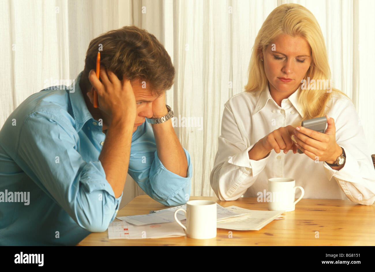 man looking distressed over bills while his partner does calculations ...