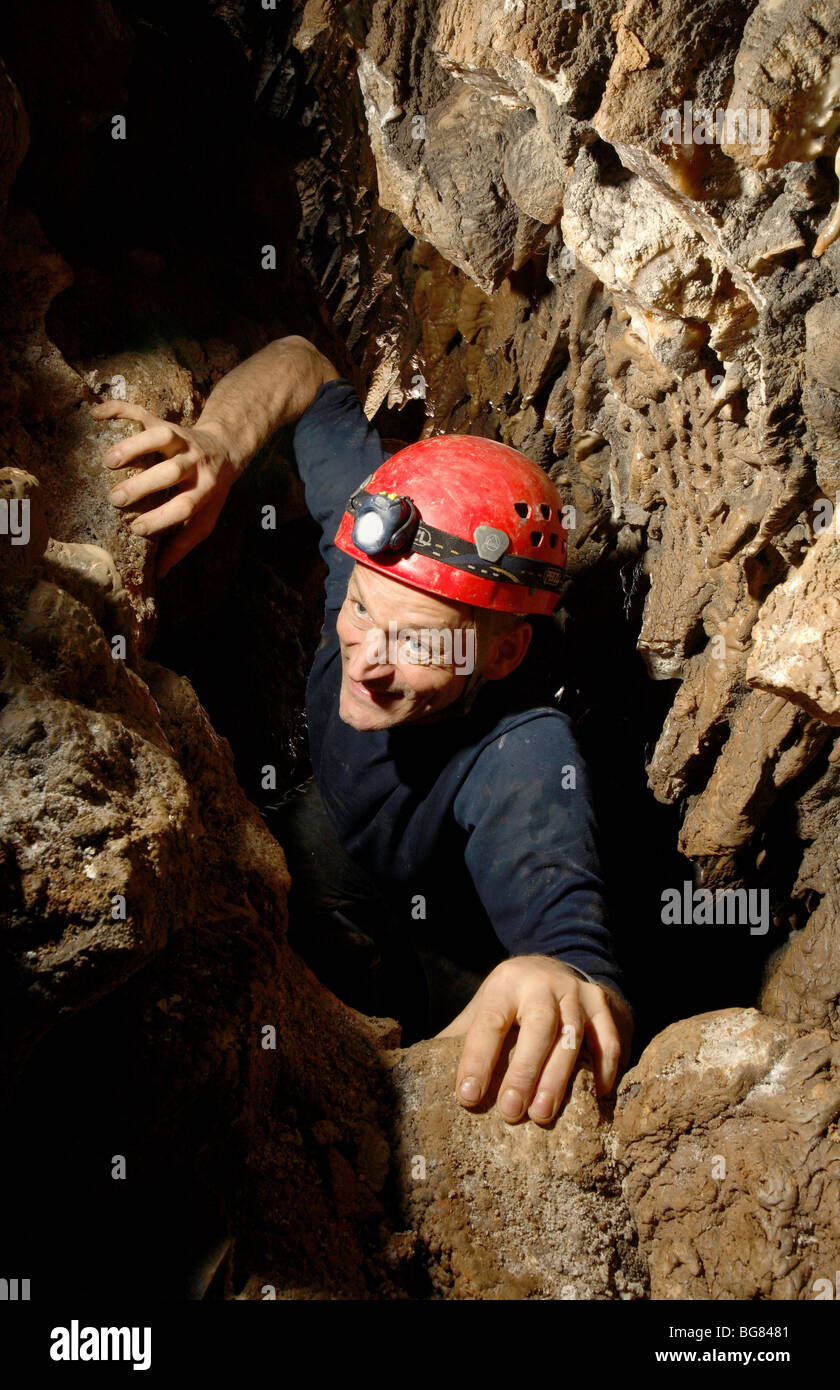 A male cave explorer squeezers up through a tight slot deep underground in Mulu National Park ...