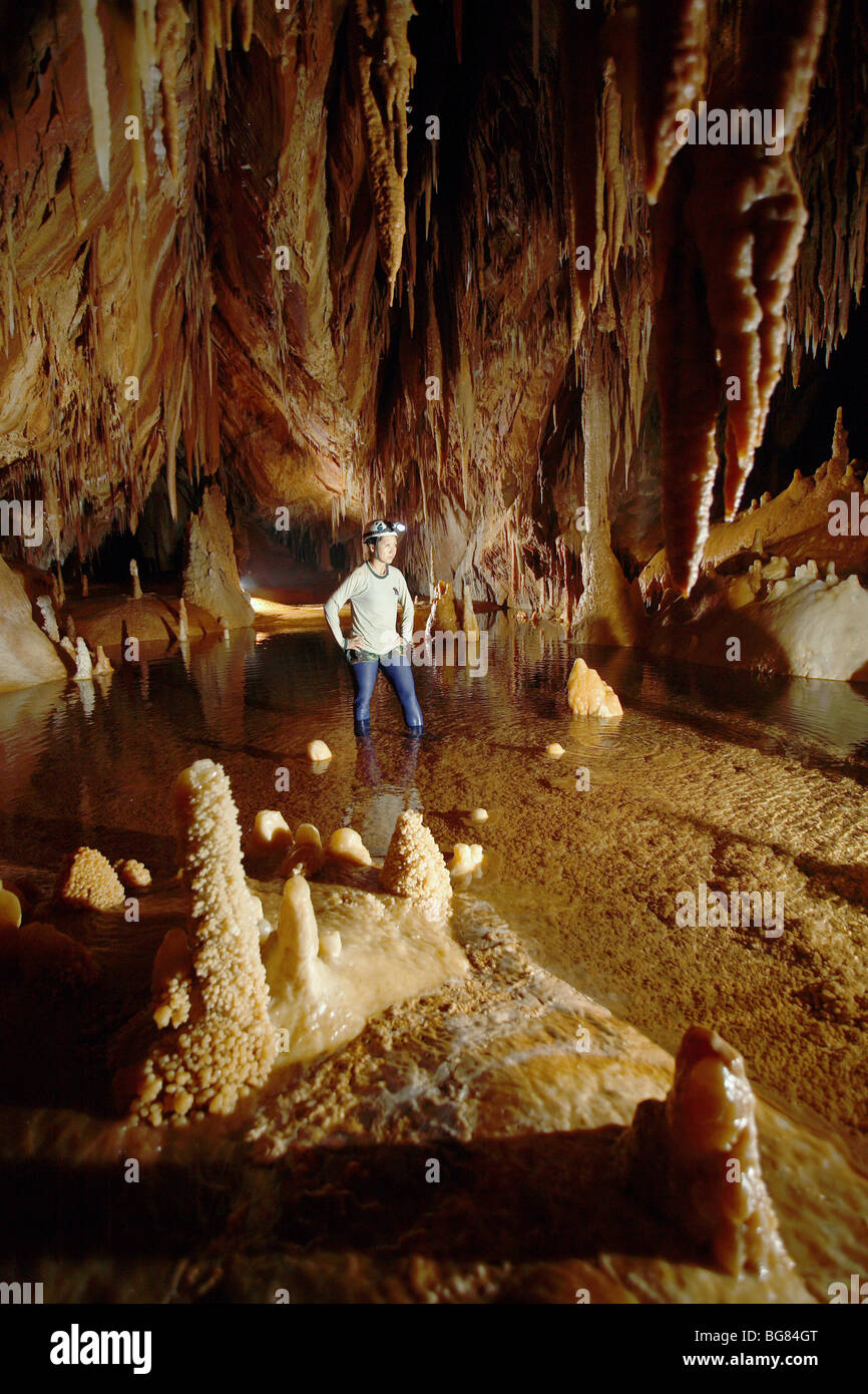 A cave explorer poses in a cave surrounded by beautiful formations ...