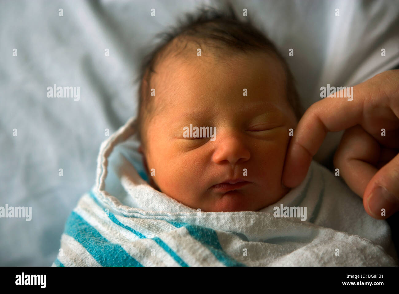 A sleeping newborn baby girl, two days old, is touched on the cheek by ...