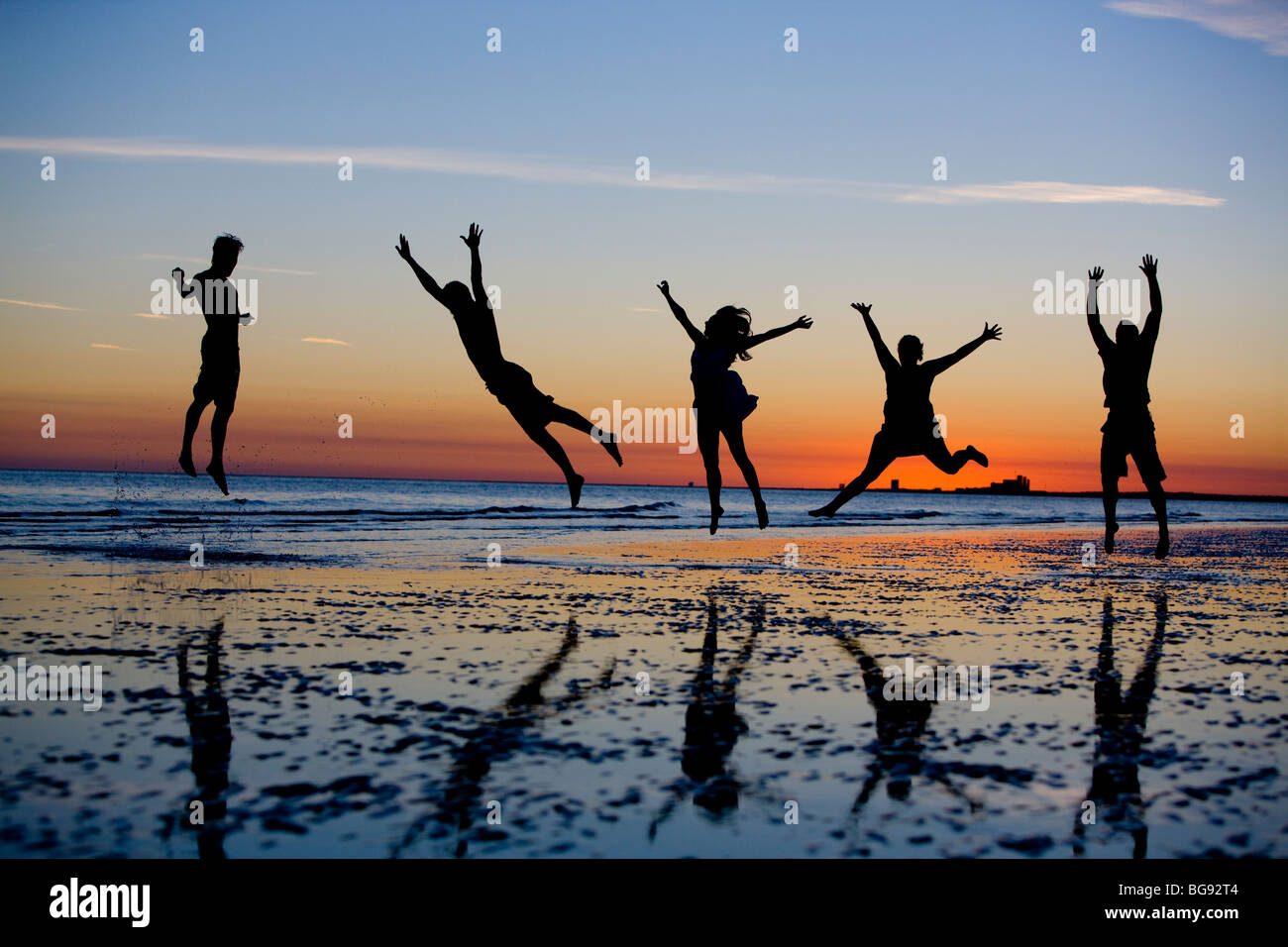 Young adults leap high during a walk on the beach Stock Photo - Alamy