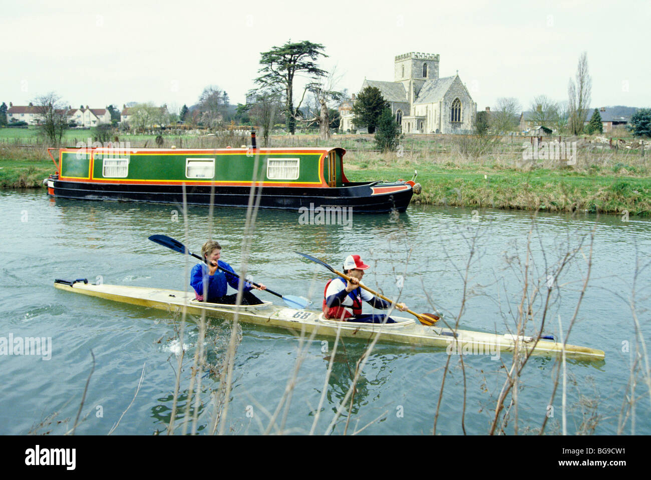 Two men kayaking past a village and houseboat Stock Photo - Alamy