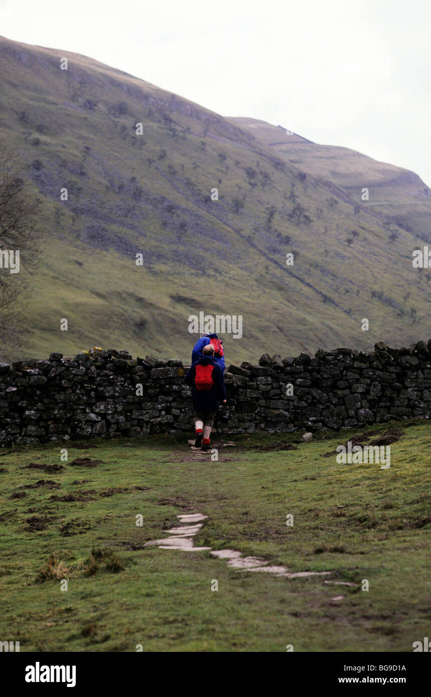 Man and woman climbing over a stone wall while fell walking in ...
