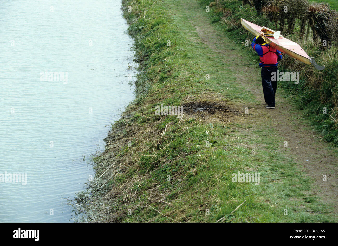 Man carrying a kayak along a river side path Stock Photo - Alamy