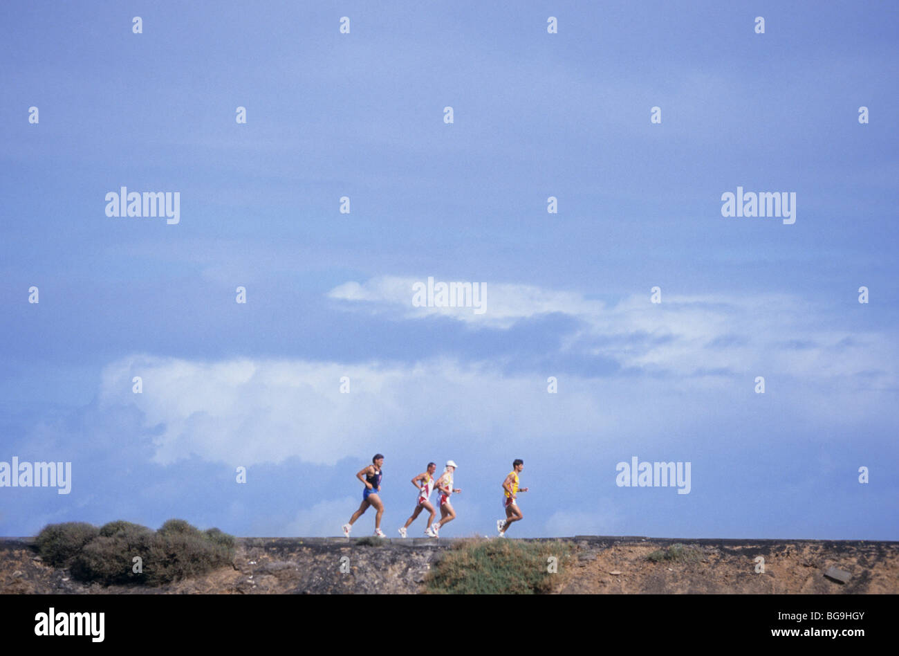 Four men jogging along a raised path Stock Photo - Alamy