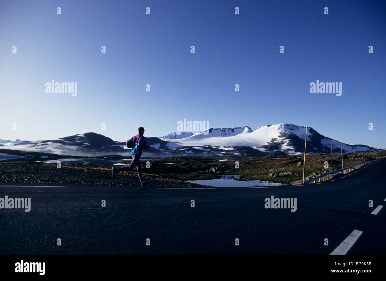 Man jogging along road by snow topped hills Stock Photo - Alamy