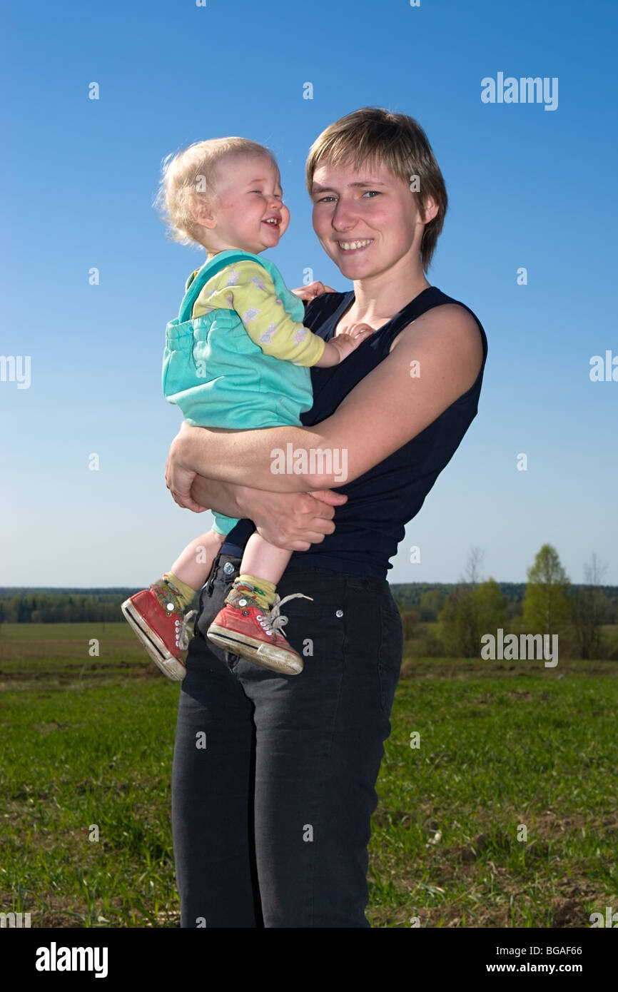 happy mother holds laughing baby on hands on a green summer meadow ...