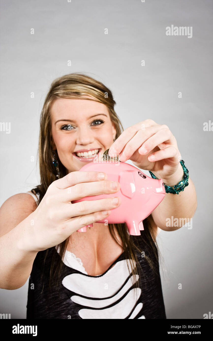young pretty woman putting money into a pink piggy bank, focus on piggy ...