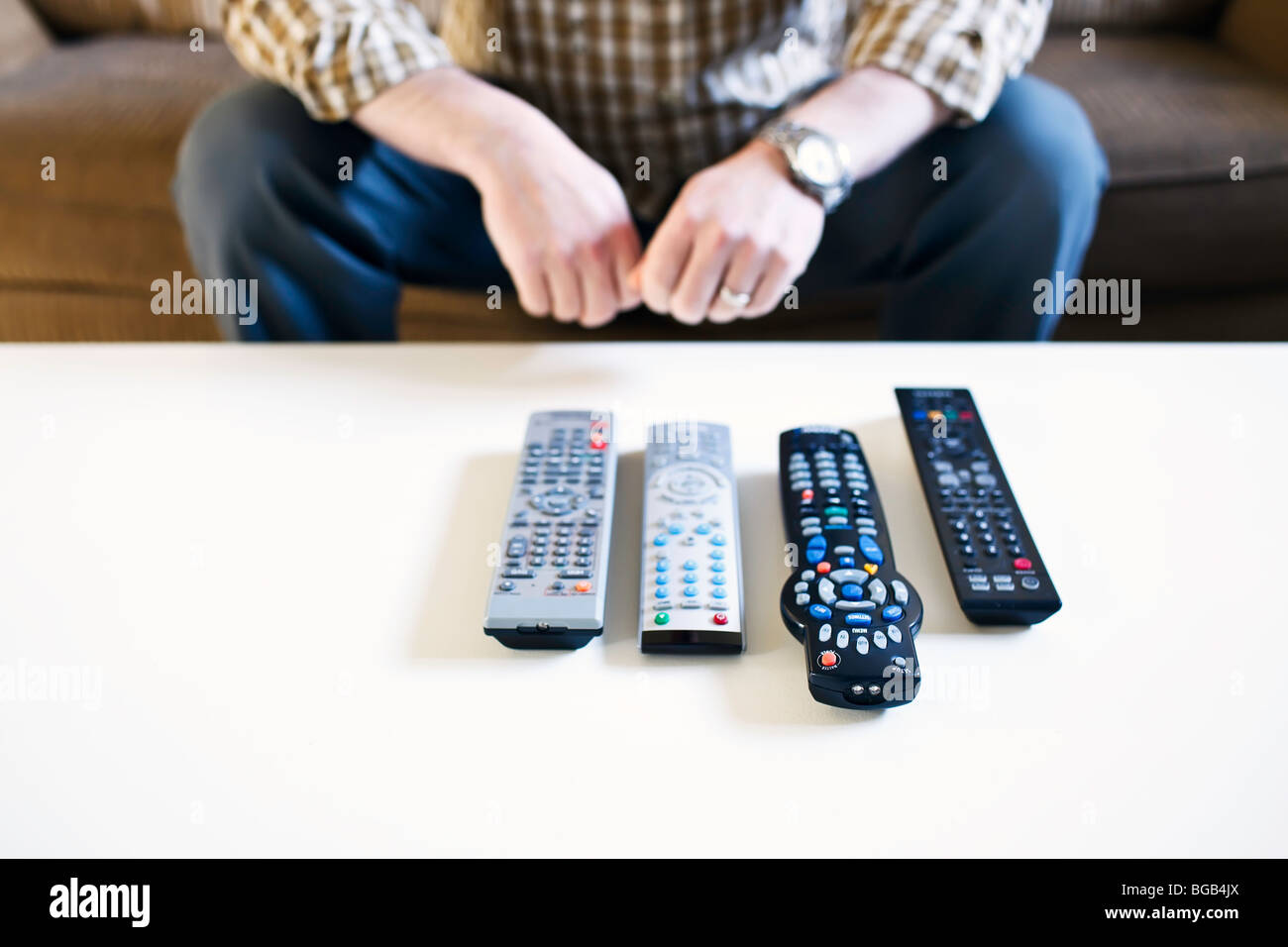 Man sitting on couch, with remote controls lined up on a coffee table ...