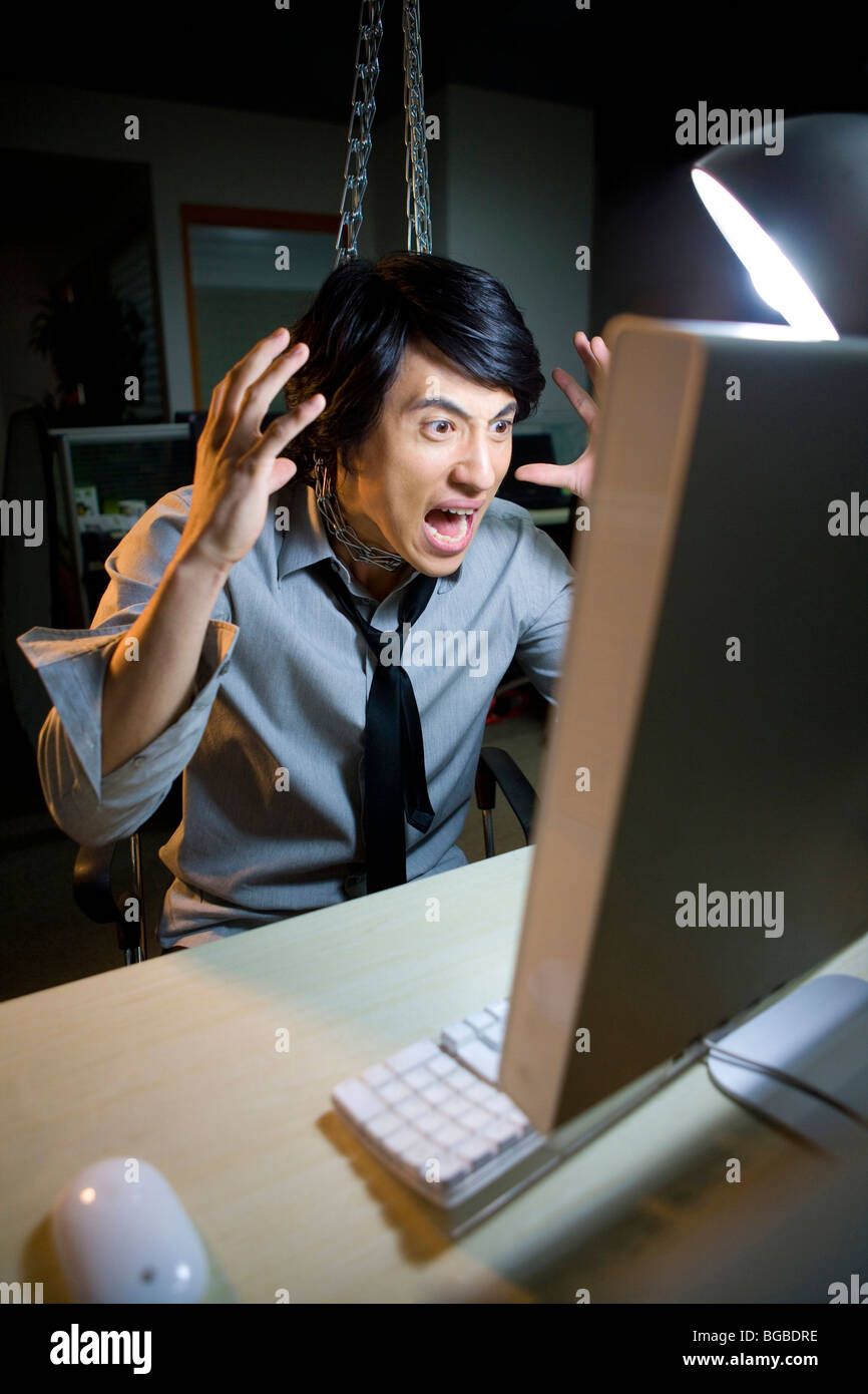 Young, infuriated man in shirt and tie is hung from a chain at his ...