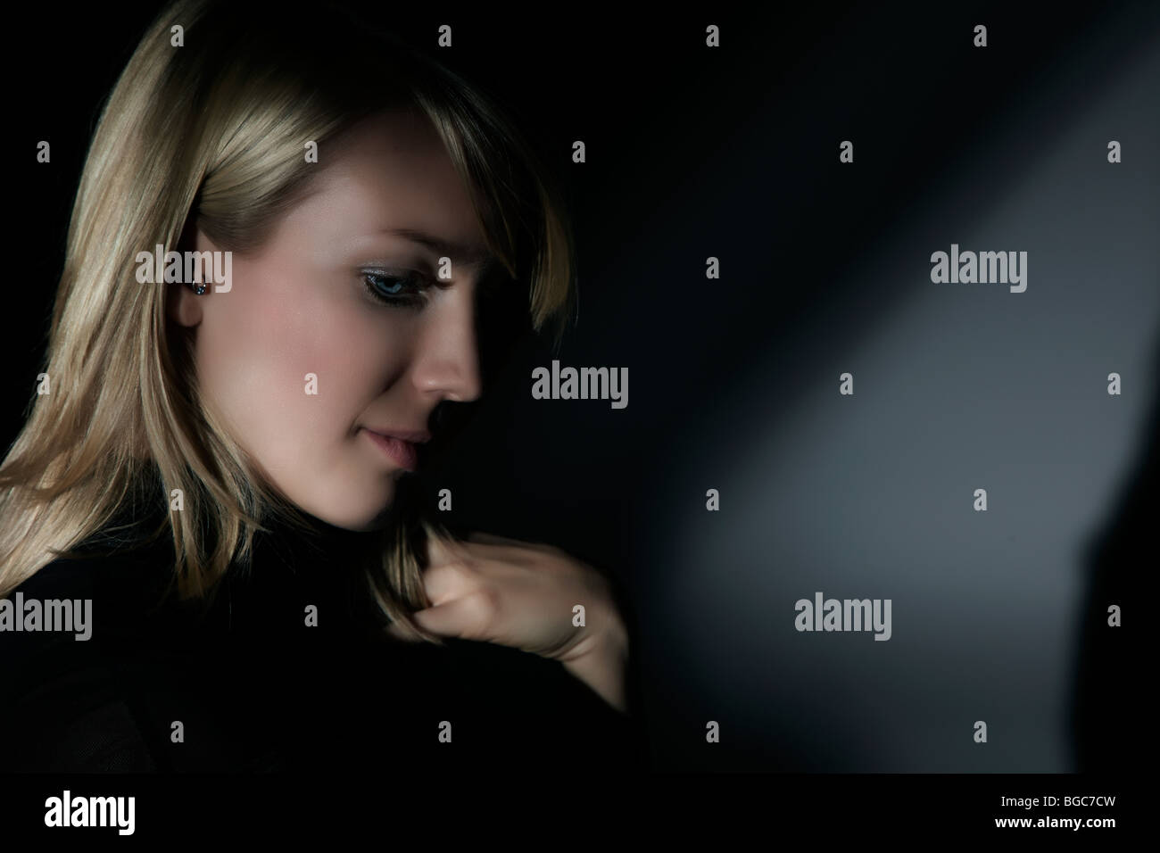 Side portrait of a young woman, surrounded by shadows, looking down ...