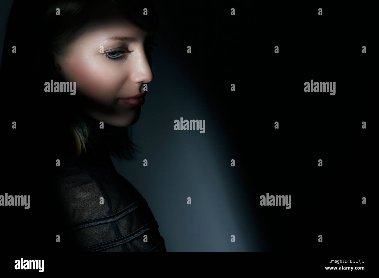 Side portrait of a young woman, surrounded by shadows, looking down ...