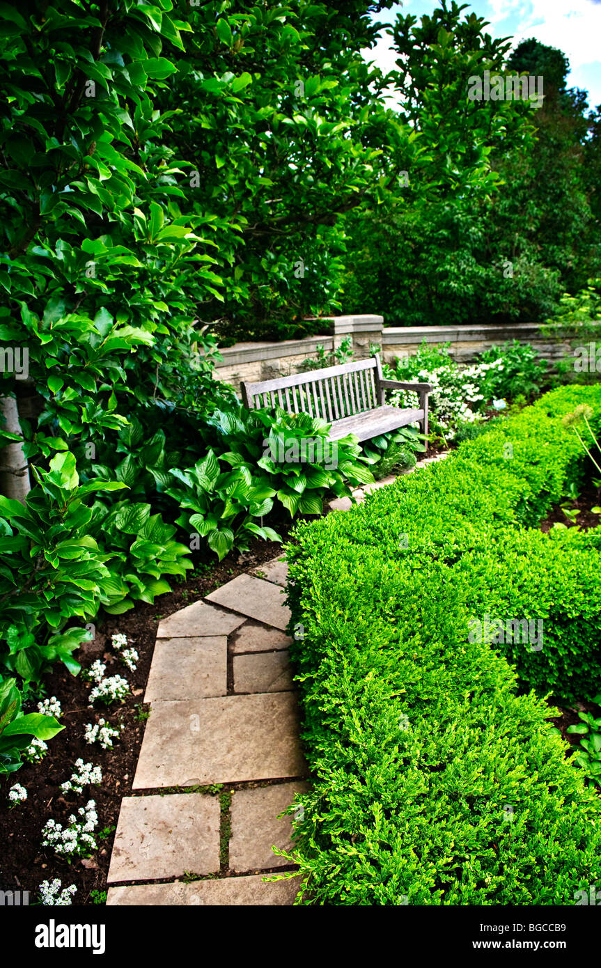 Lush green garden with stone landscaping, hedge, path and bench Stock ...