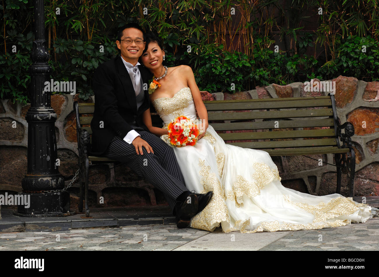 Chinese bride and groom in long wedding gown and dark suit sitting on a ...