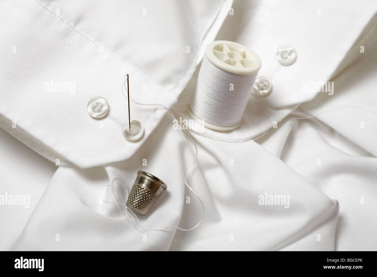 Spool of thread, needle and old thimble on white shirt Stock Photo - Alamy