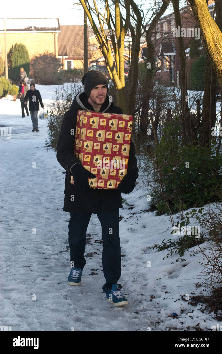 Young man carrying a wrapped Christmas present in the snow and Ice ...