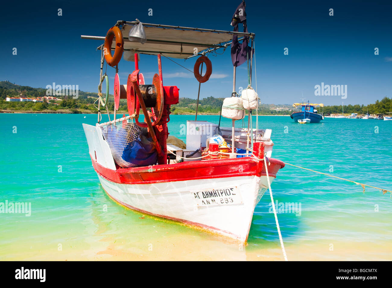 A red and white painted fishing boat is moored on a beach in a lagoon ...