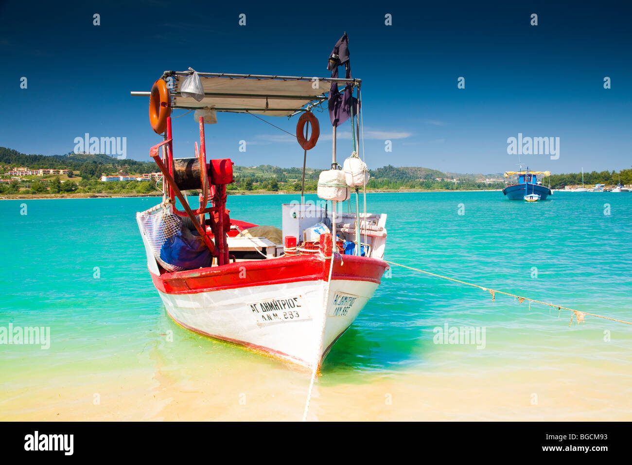 A red and white painted fishing boat is moored on a beach in a lagoon ...