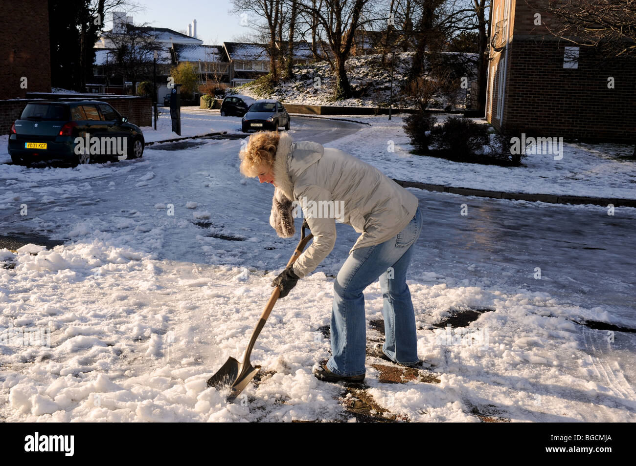 Woman clearing snow and ice from her path and drive using a shovel in ...