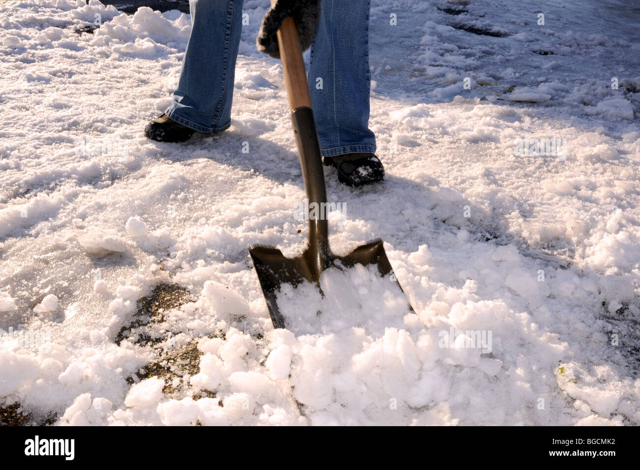 Woman clearing snow and ice from her path and drive using a shovel in ...