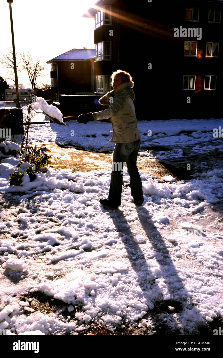 Woman clearing snow and ice from her path and drive using a shovel in ...