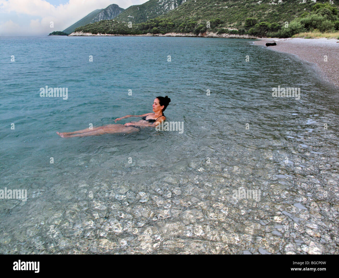 Woman relaxes, swims in clear transparent sea water. Pebbled beach in ...