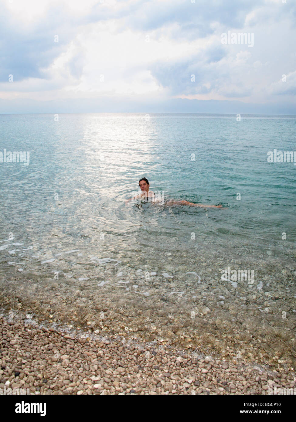 Woman relaxes, swims in clear transparent sea water. Pebbled beach in ...