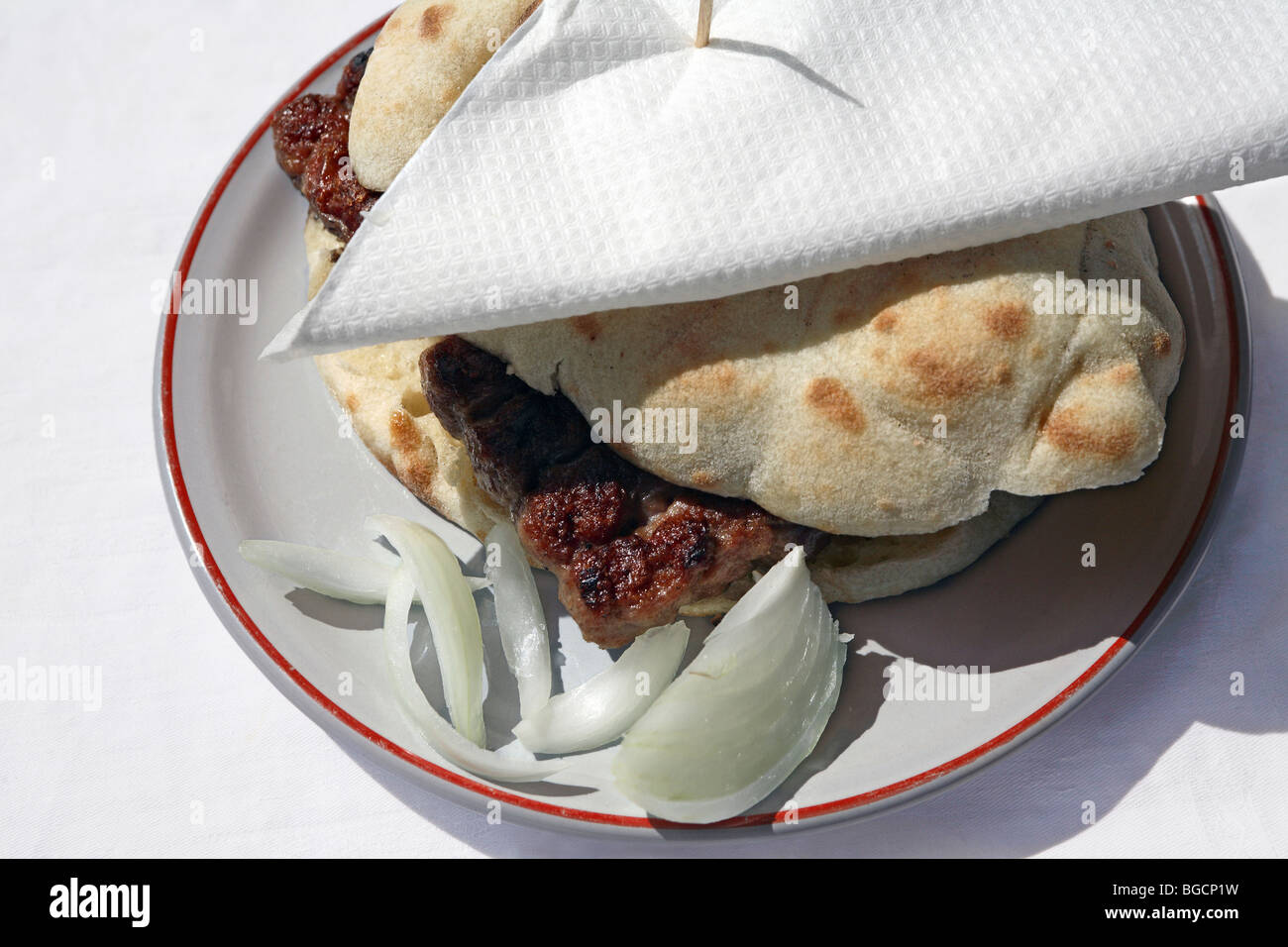 Cevapcici in bread with sliced onion served on a plate. Bosnia, Bosnian ...
