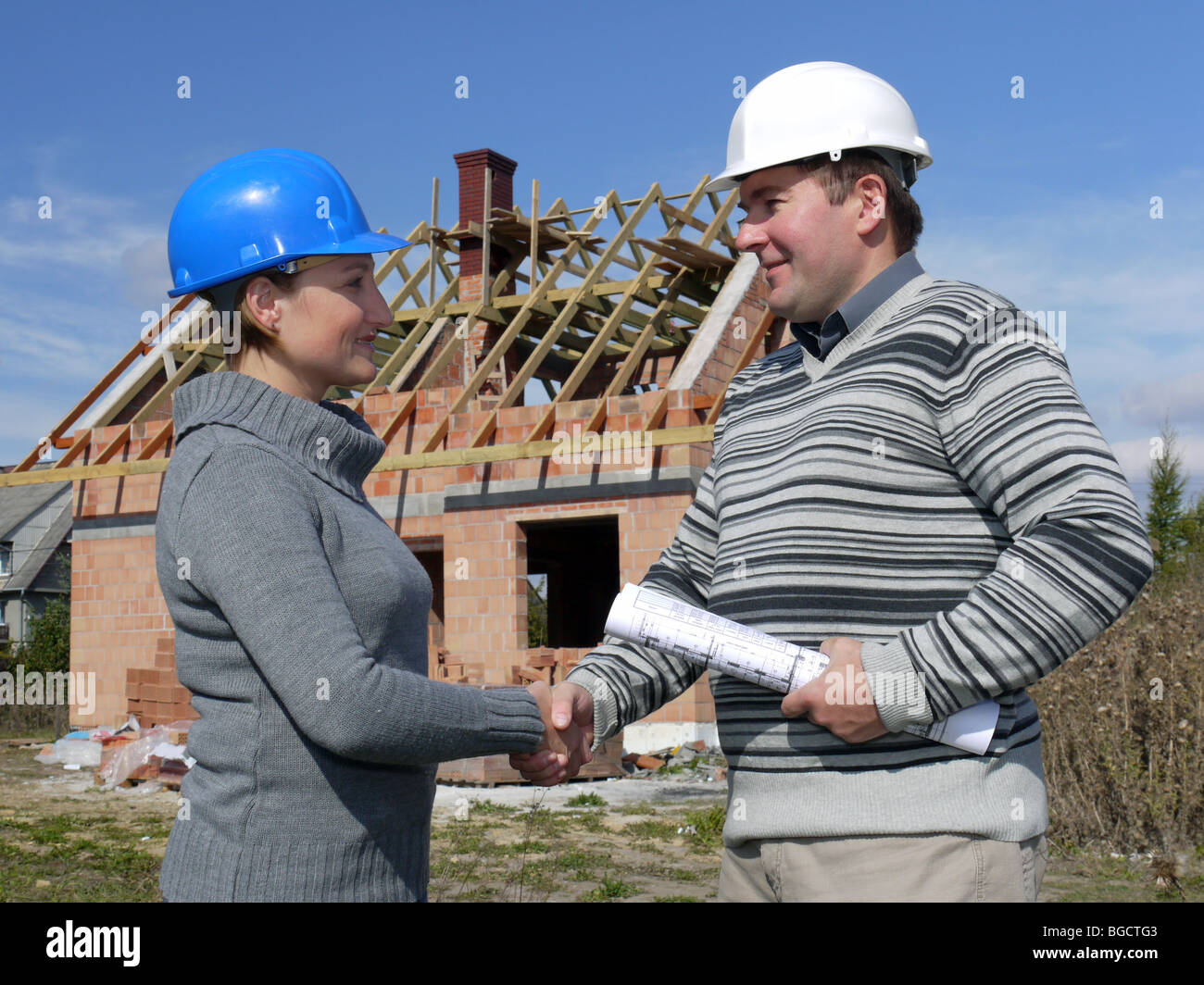 Female and male building engineers standing against unfinished brick ...