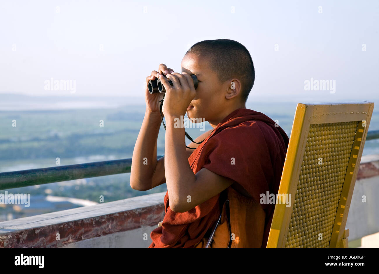 Young novice monk looking through binoculars. Mandalay Hill viewpoint ...