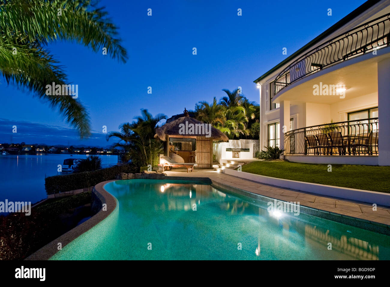 Luxurious mansion exterior at dusk overlooking pool, canal and Bali hut ...