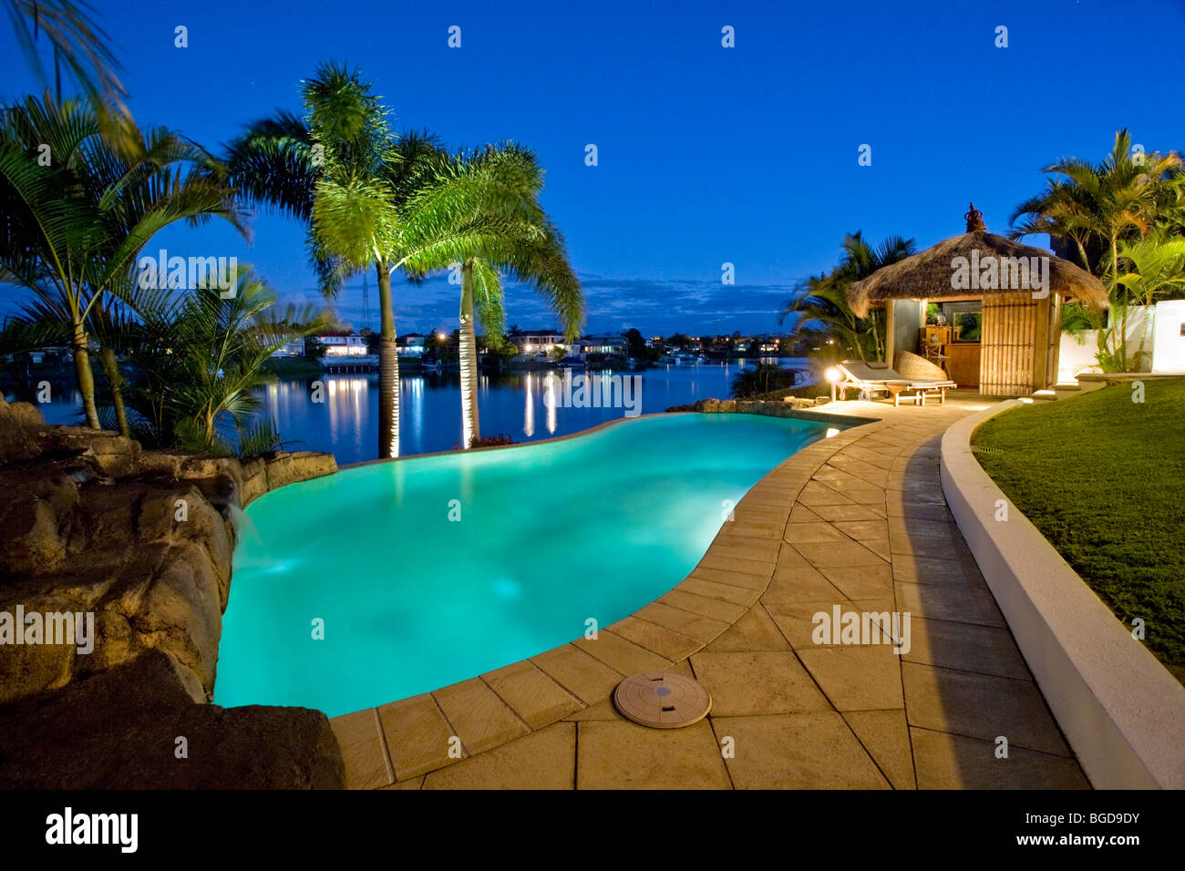 Luxurious mansion exterior at dusk overlooking pool, canal and Bali hut ...