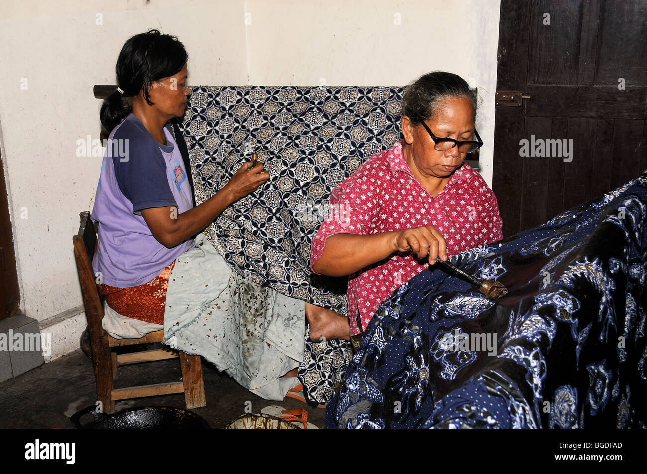Women applying wax with a canting tool on a pattern in a batik factory ...