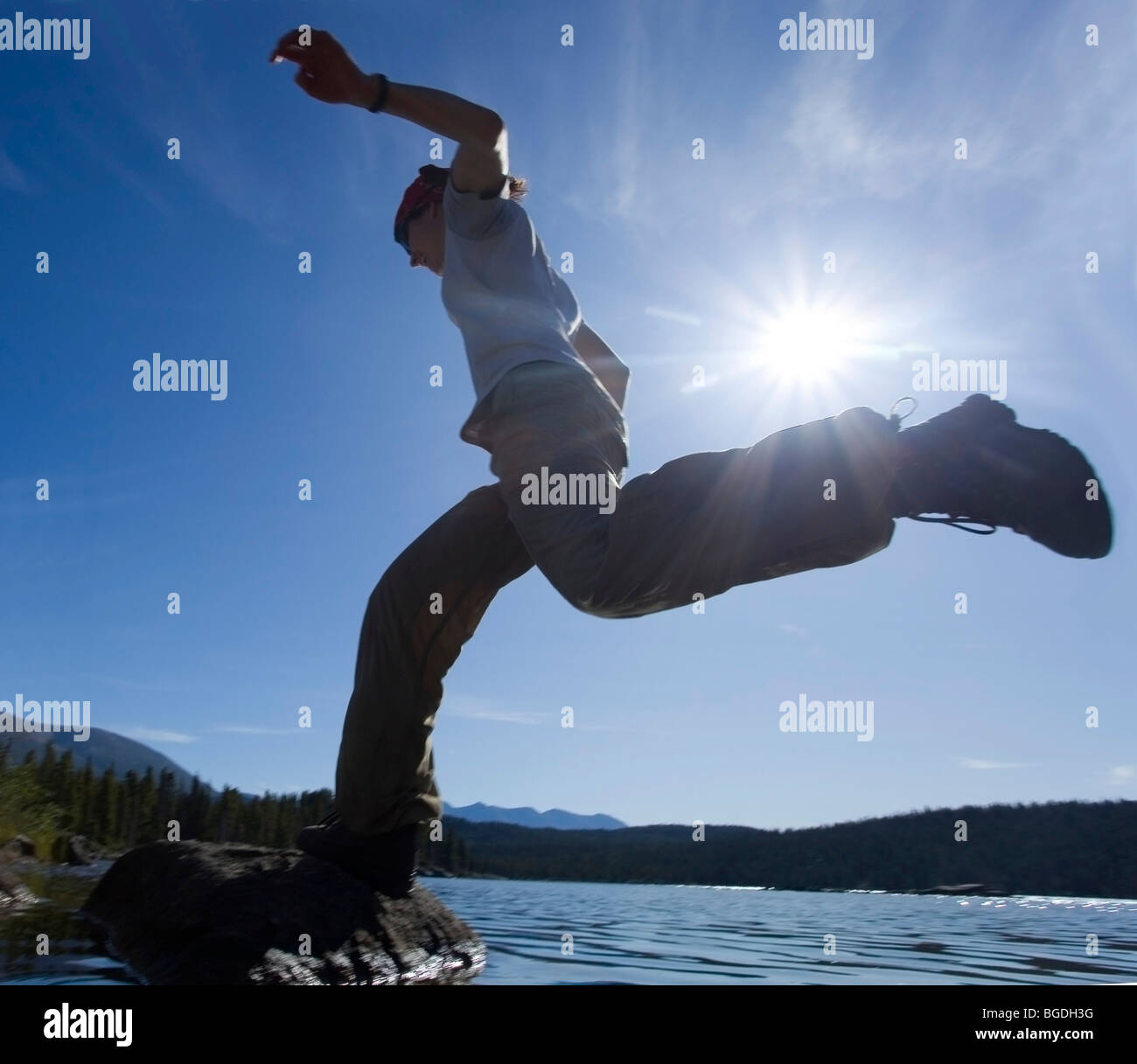 Silhouette of a young woman jumping across a creek, hiking, backpacking ...