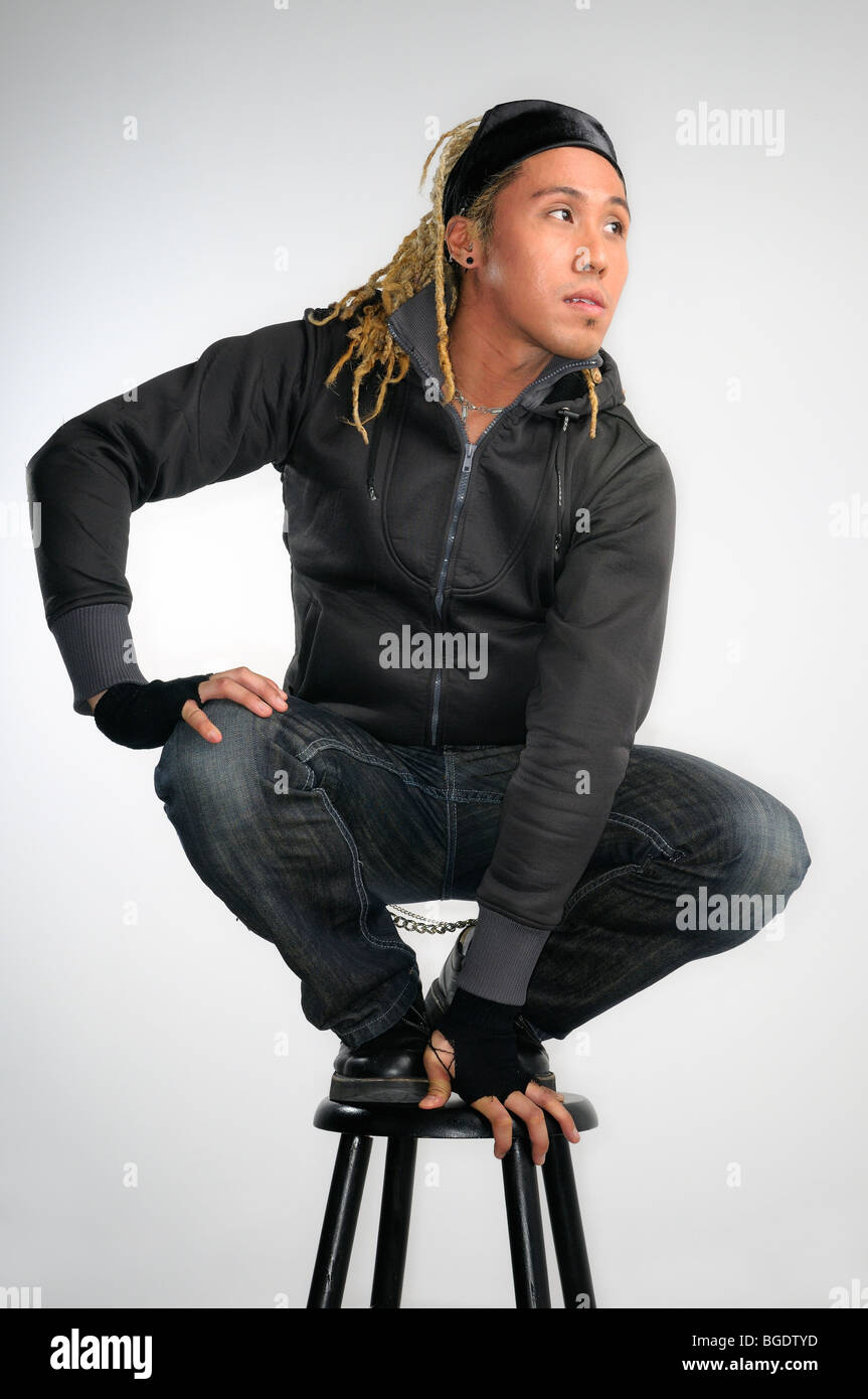 Asian man with dreadlocks crouching on a stool on white background ...