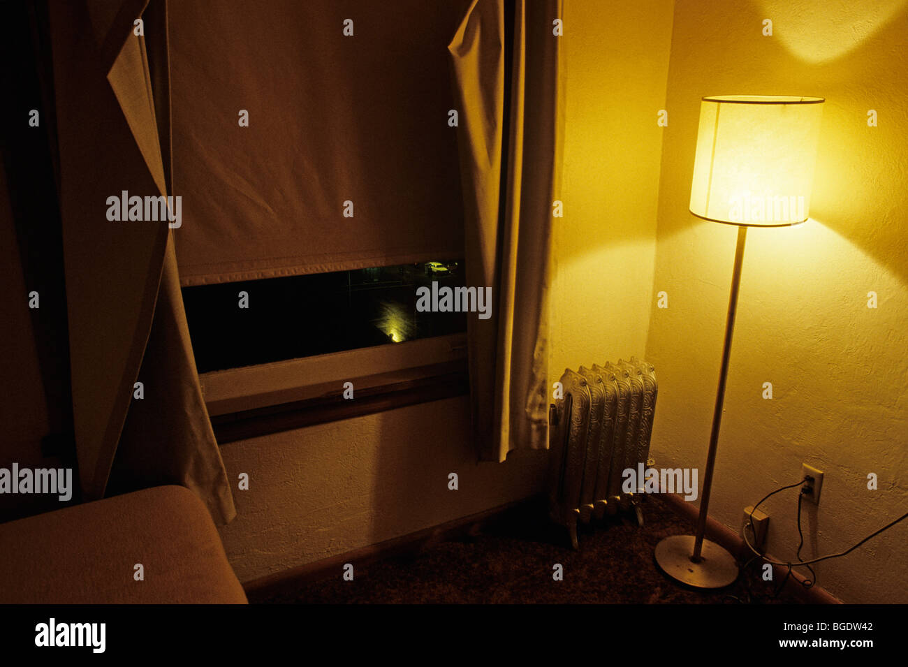 Hotel room at night with focus on window with torn shades and lamp ...