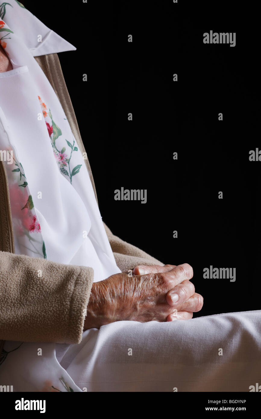 Elderly woman sitting with hands clasped on lap. Isolated. Copy space ...