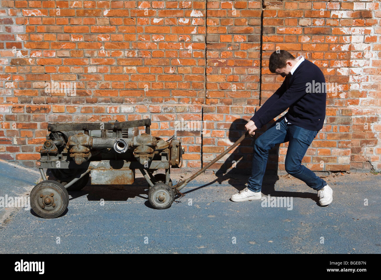 A boy trying and failing to drag an old and rusty engine Stock Photo ...
