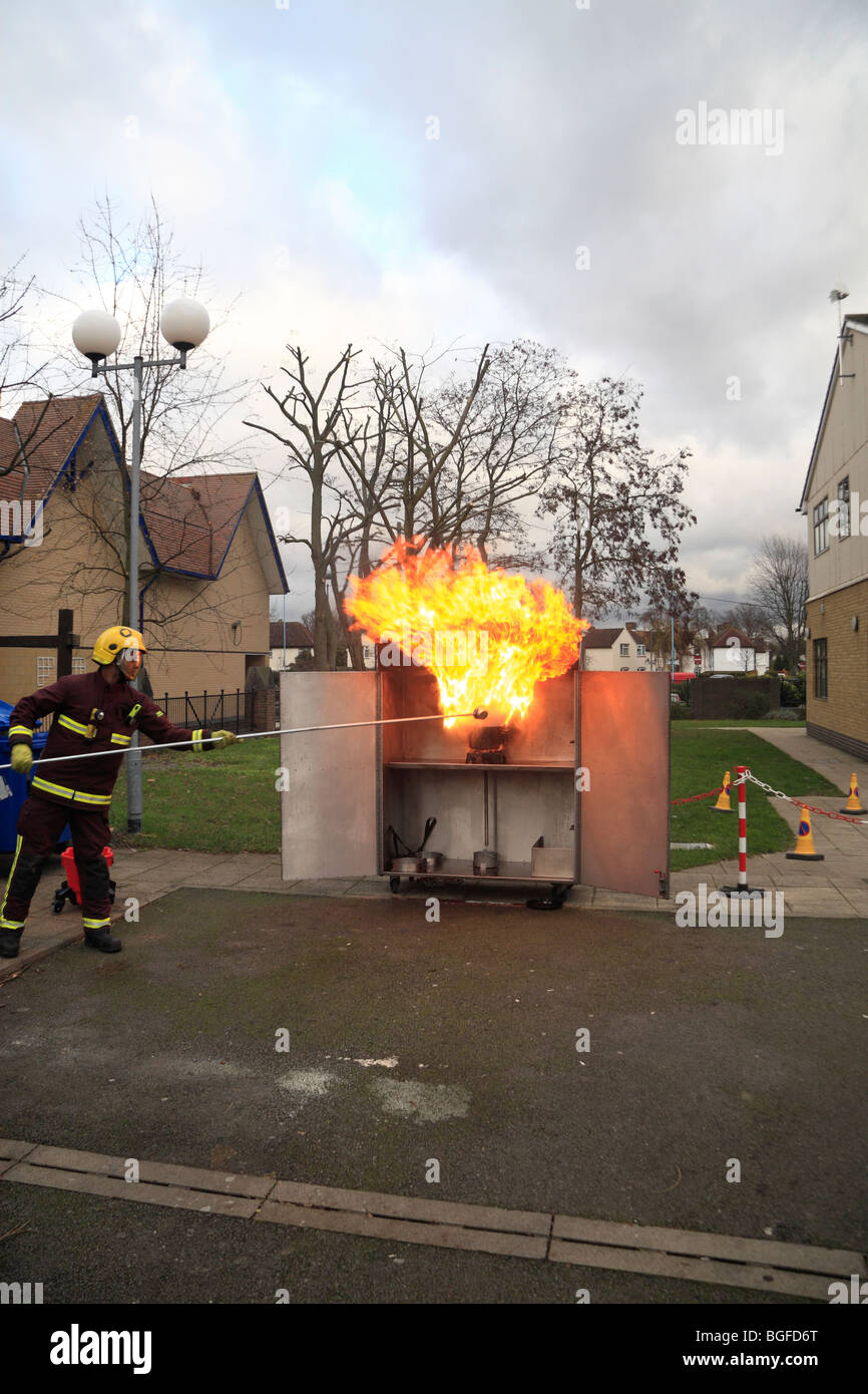 A London Fire Brigade Fireman puts water into a burning oil filled pan ...