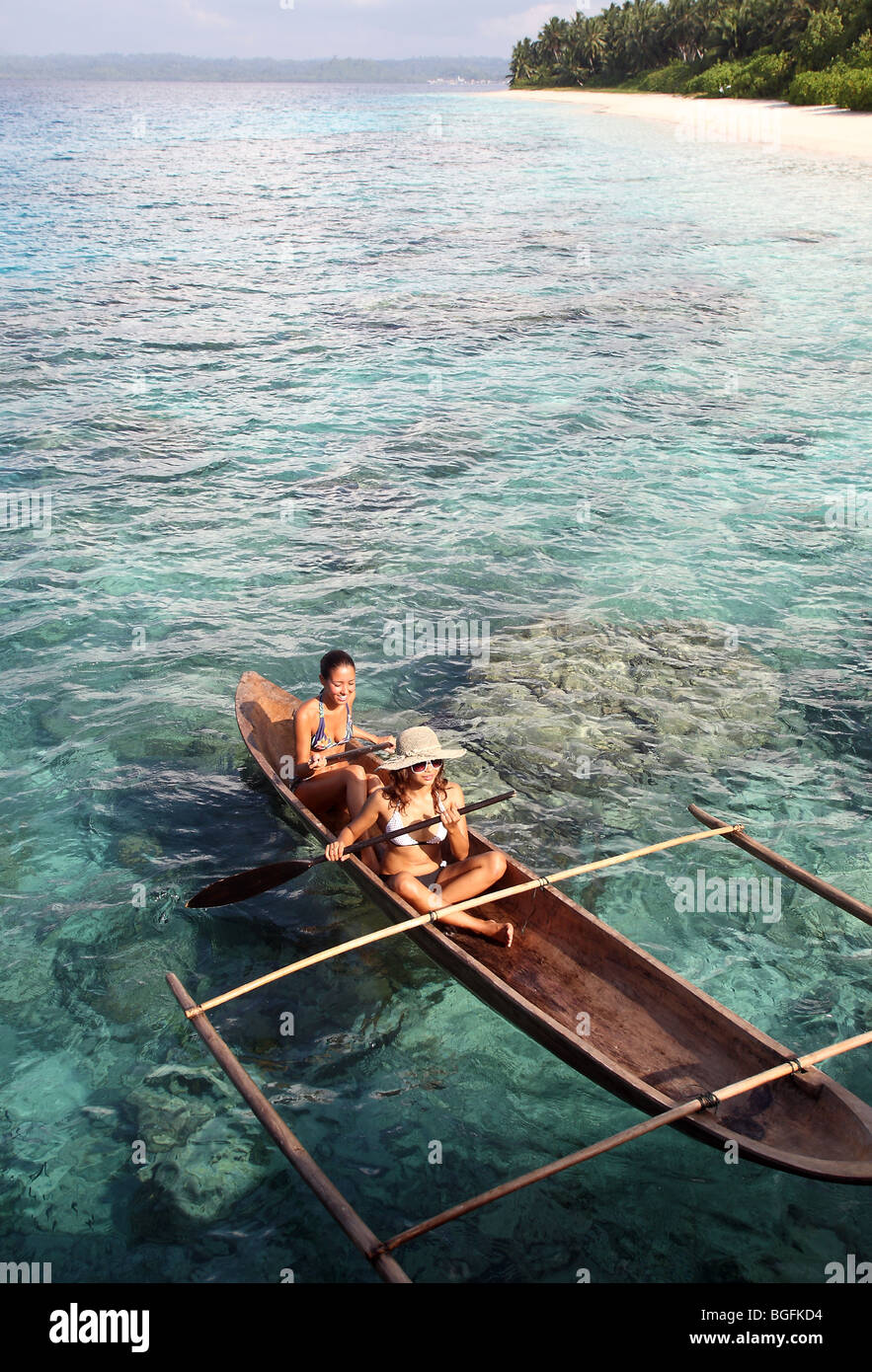 Two young woman paddling an outrigger canoe. Mentawai Islands, Sumatra ...