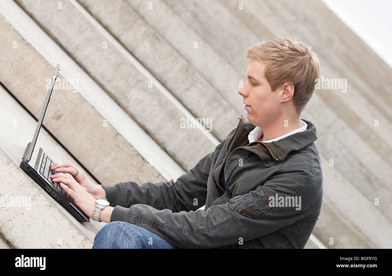 Young blond handsome smiling guy sitting outdoors with laptop computer ...