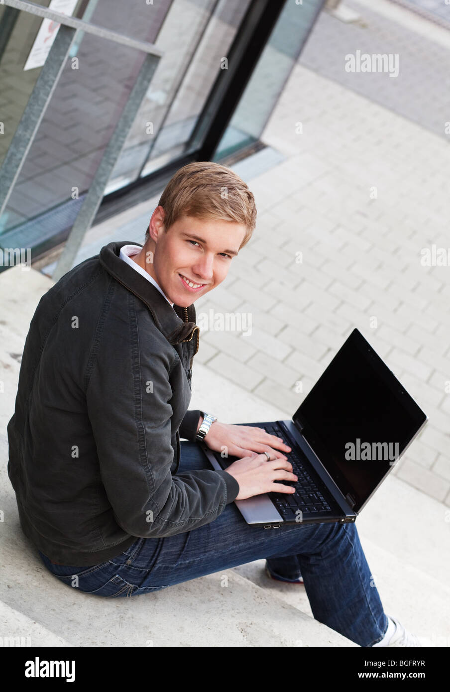Young blond handsome smiling guy sitting outdoors with laptop computer ...
