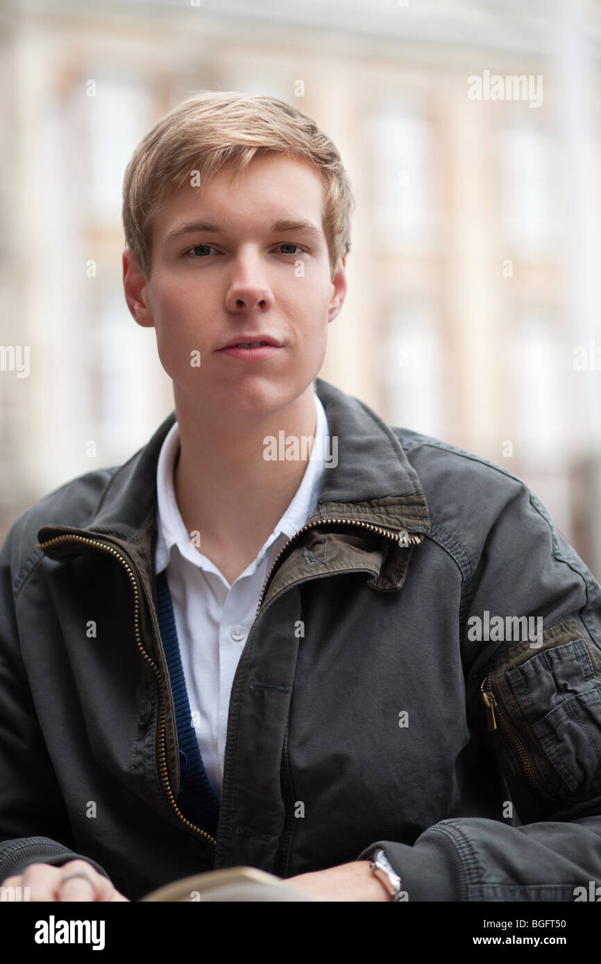Portrait of a young handsome blond man sitting outdoors with a book ...